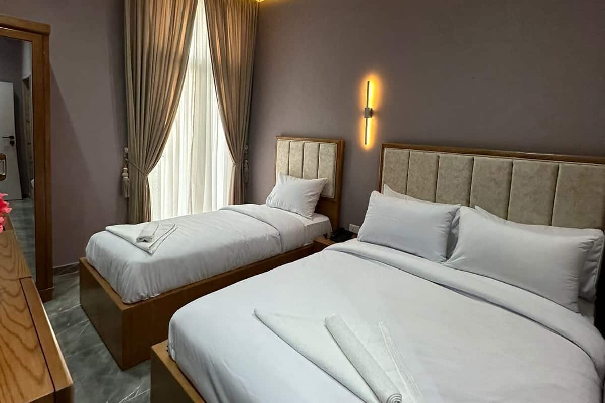 Quarto de hotel com duas camas, uma mesa de cabeceira de madeira, um espelho e uma janela com cortinas.