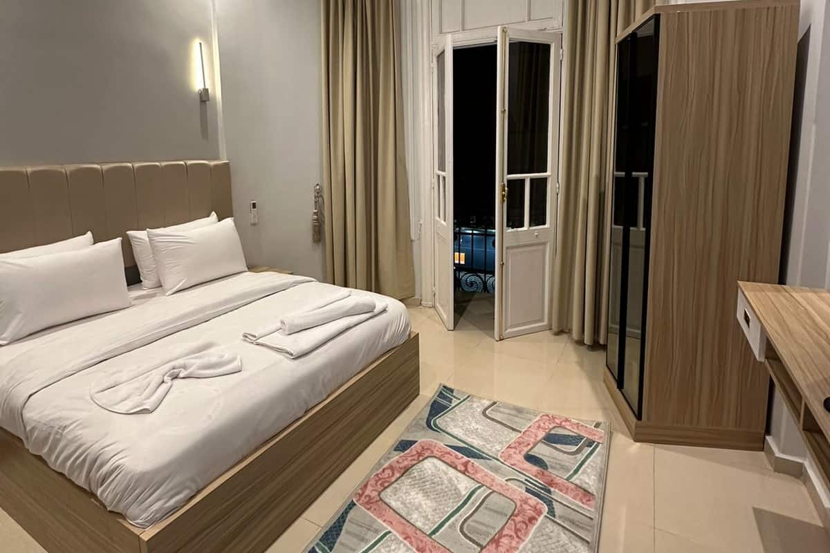 Quarto de hotel moderno com uma cama grande, cabeceira de madeira, escrivaninha e guarda-roupa.