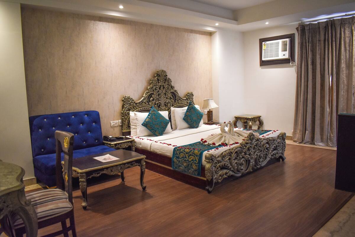 Quarto com uma cama grande, uma poltrona azul estofada, uma mesa pequena e um criado-mudo.