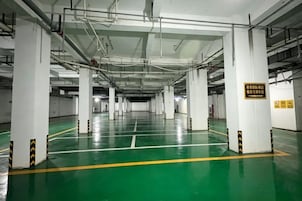 Um estacionamento multi andar com pilares brancos, piso verde e linhas amarelas delimitando as vagas.