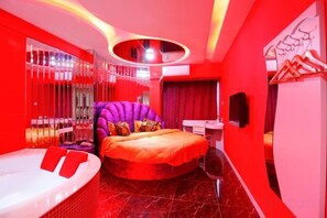 Quarto com cama grande, hidromassagem circular e decoração em tons de vermelho.