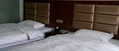 Quarto de hotel com duas camas, cabeceira de madeira e mesa de cabeceira com abajur.