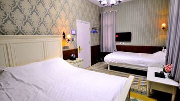 Quarto de hotel com duas camas, televisão, uma mesinha com um vaso e papel de parede estampado.