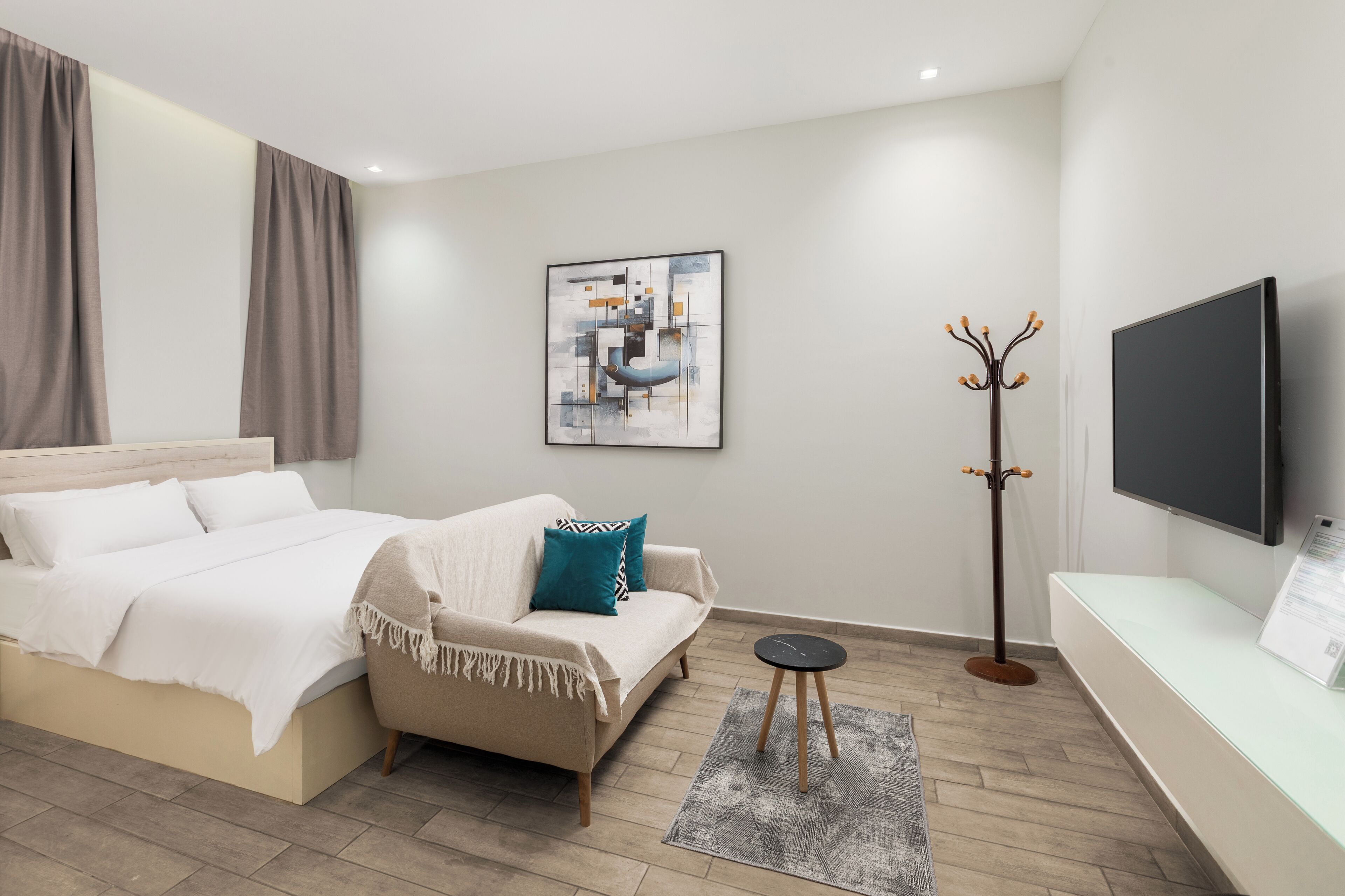 Quarto de hotel moderno com cama, sofá, televisão de tela plana, cabideiro e um quadro na parede.