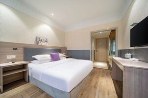 Quarto de hotel moderno com uma cama grande, cabeceira de madeira, mesas de cabeceira, televisão de tela plana e uma kitchenette.