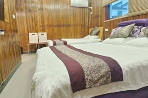 Quarto de hotel com painéis de madeira, duas camas com roupa de cama estampada, uma janela com persianas e um ar condicionado fixado na parede.