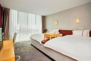 Quarto de hotel com duas camas, uma escrivaninha, uma cadeira, uma mesa e uma janela grande com cortinas.