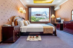 Quarto de hotel com cama, mesa de cabeceira, cômoda, televisão e janela com vista para as montanhas.