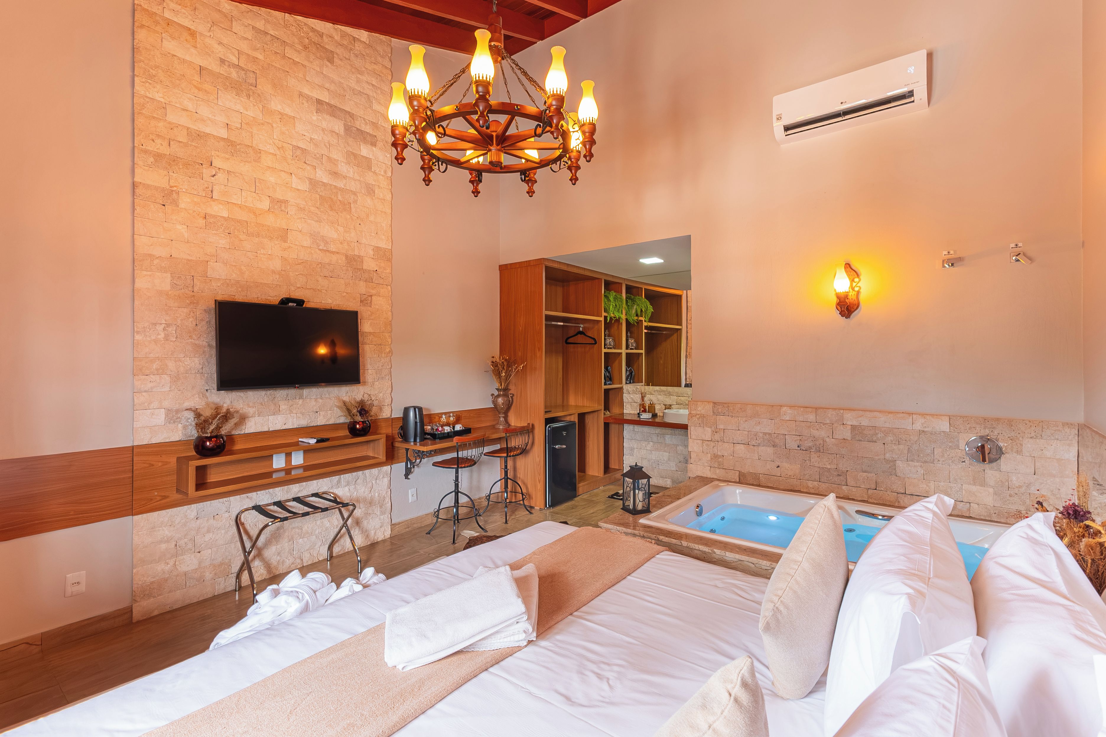 Quarto de hotel com uma cama grande, área de estar com mesa e cadeiras, pequena cozinha e banheiro com banheira.