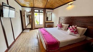 Um quarto com cama de madeira, ventilador de teto, televisão e janela com cortinas.