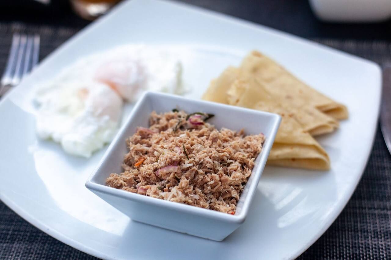Um prato com carne desfiada, acompanhado de ovos fritos e uma tortilla dobrada.