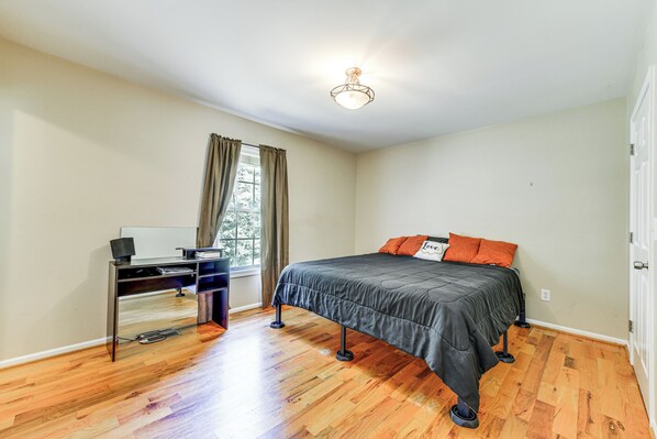 Quarto com cama, escrivaninha e janela com cortinas.