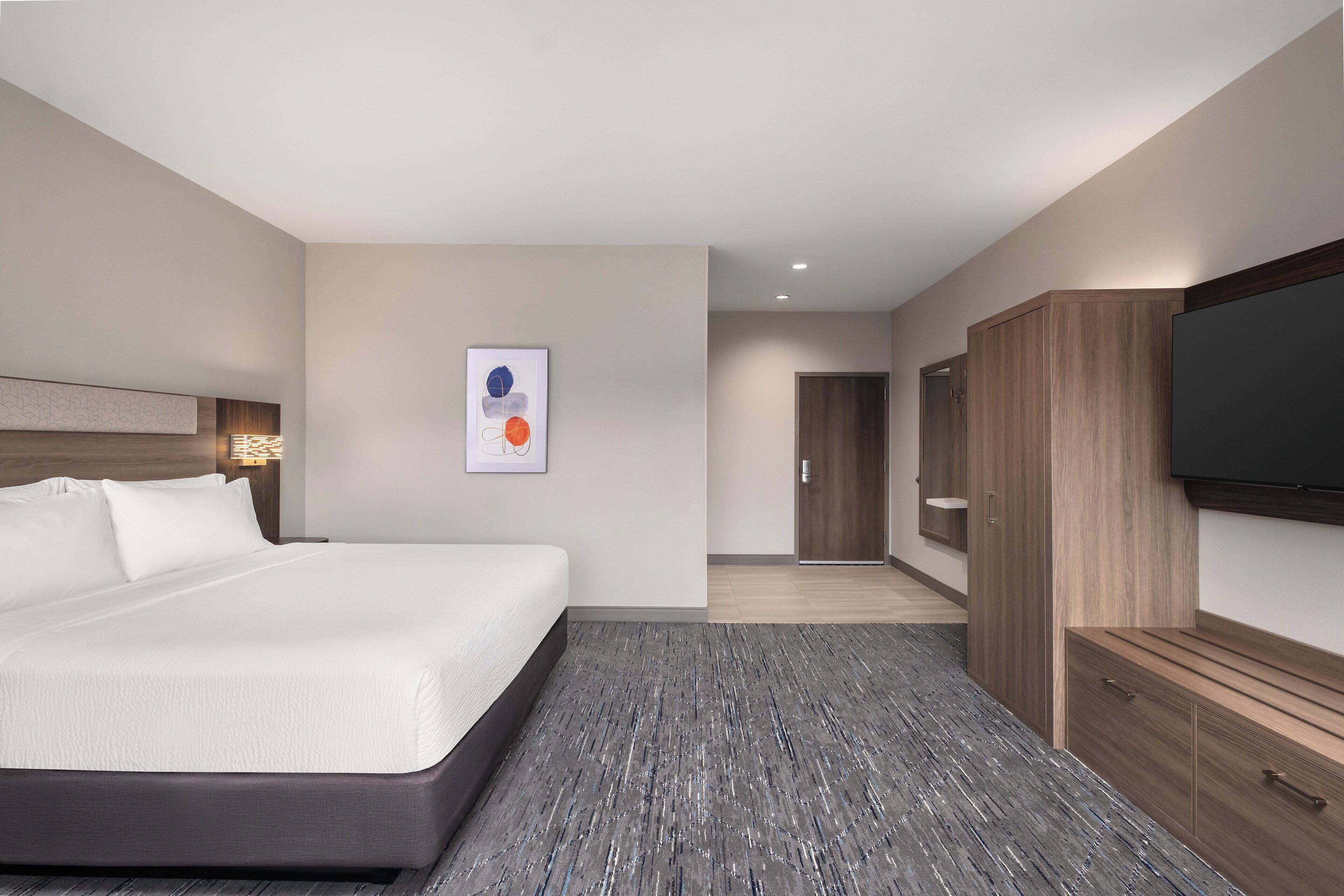 Quarto de hotel moderno com uma cama grande, televisão de tela plana, guarda-roupa e uma obra de arte emoldurada na parede.