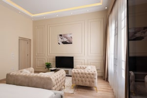 Uma sala de estar moderna com televisão de tela plana, dois sofás estofados, uma mesa de centro e uma janela grande com cortinas.