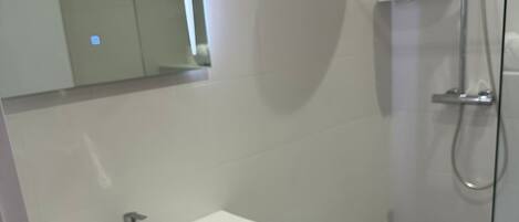 Uma casa de banho moderna com cabine de chuveiro em vidro, lavatório branco e espelho grande.