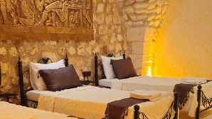 Quarto de hotel com três camas, cada uma com um estilo diferente de cabeceira e travesseiros. O quarto possui paredes de pedra e um grande mural acima das camas.