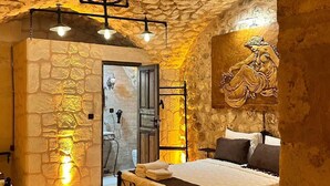 Quarto com paredes de pedra, uma cama, luminária pendente e um quadro na parede.