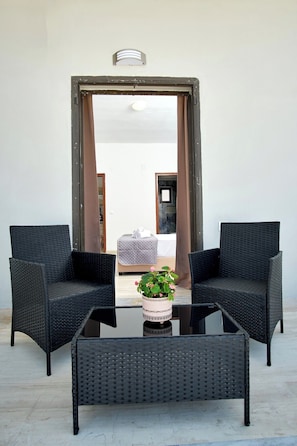 Quarto com duas cadeiras de vime, uma mesinha e um vaso de planta.