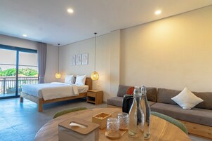 Quarto de hotel moderno com cama grande, sofá, mesa de jantar e varanda com vista para o verde.
