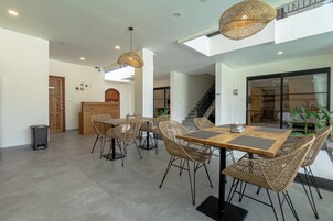 Uma área de refeições moderna com cadeiras de vime, uma mesa de madeira, uma escada e uma grande janela.