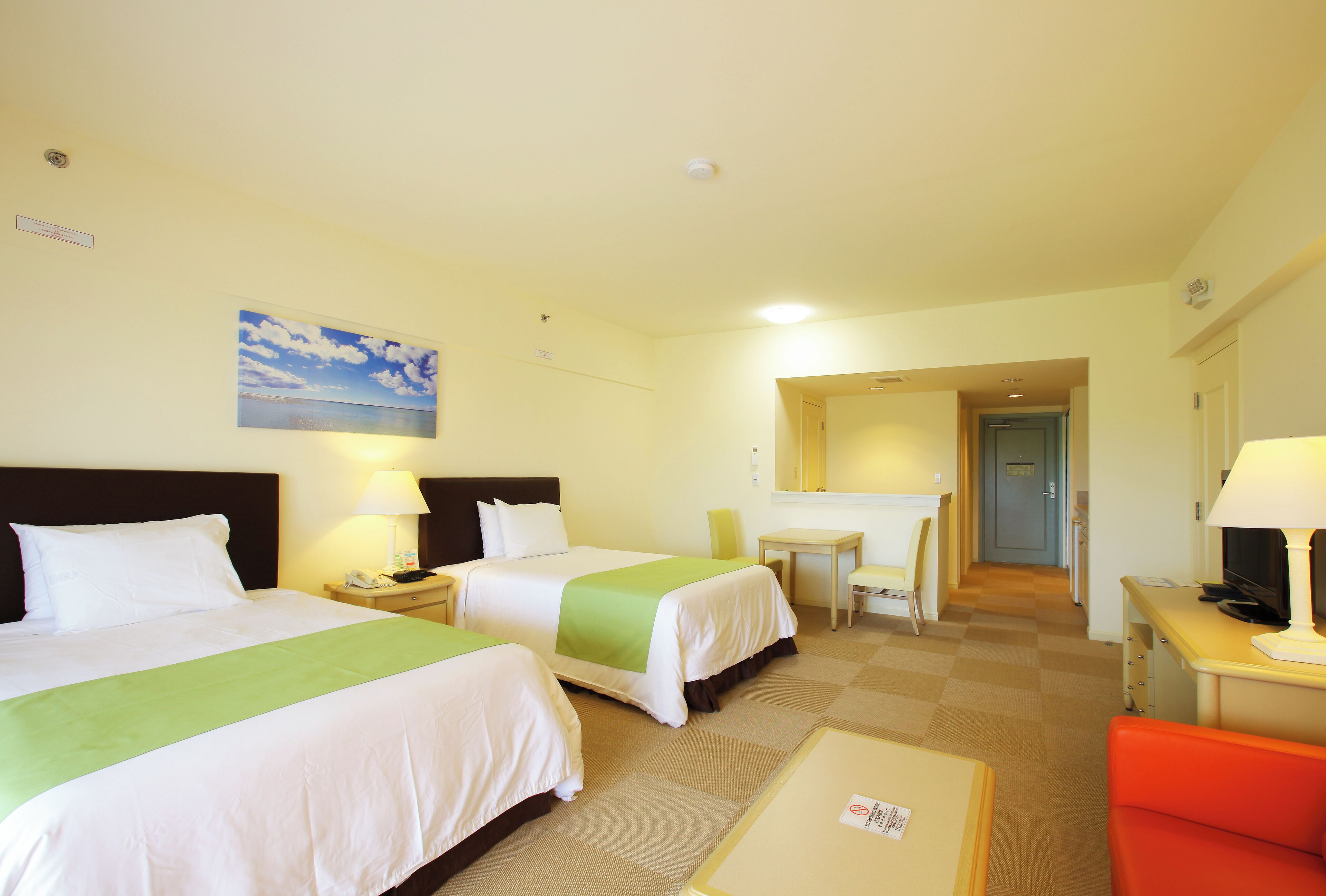 Quarto de hotel com duas camas, uma escrivaninha, uma cadeira e uma televisão.