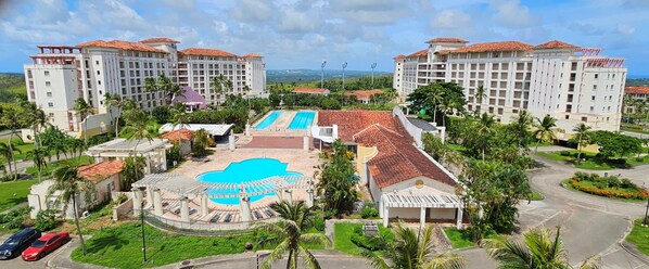 Resort com vários edifícios, piscina central e vegetação ao redor.