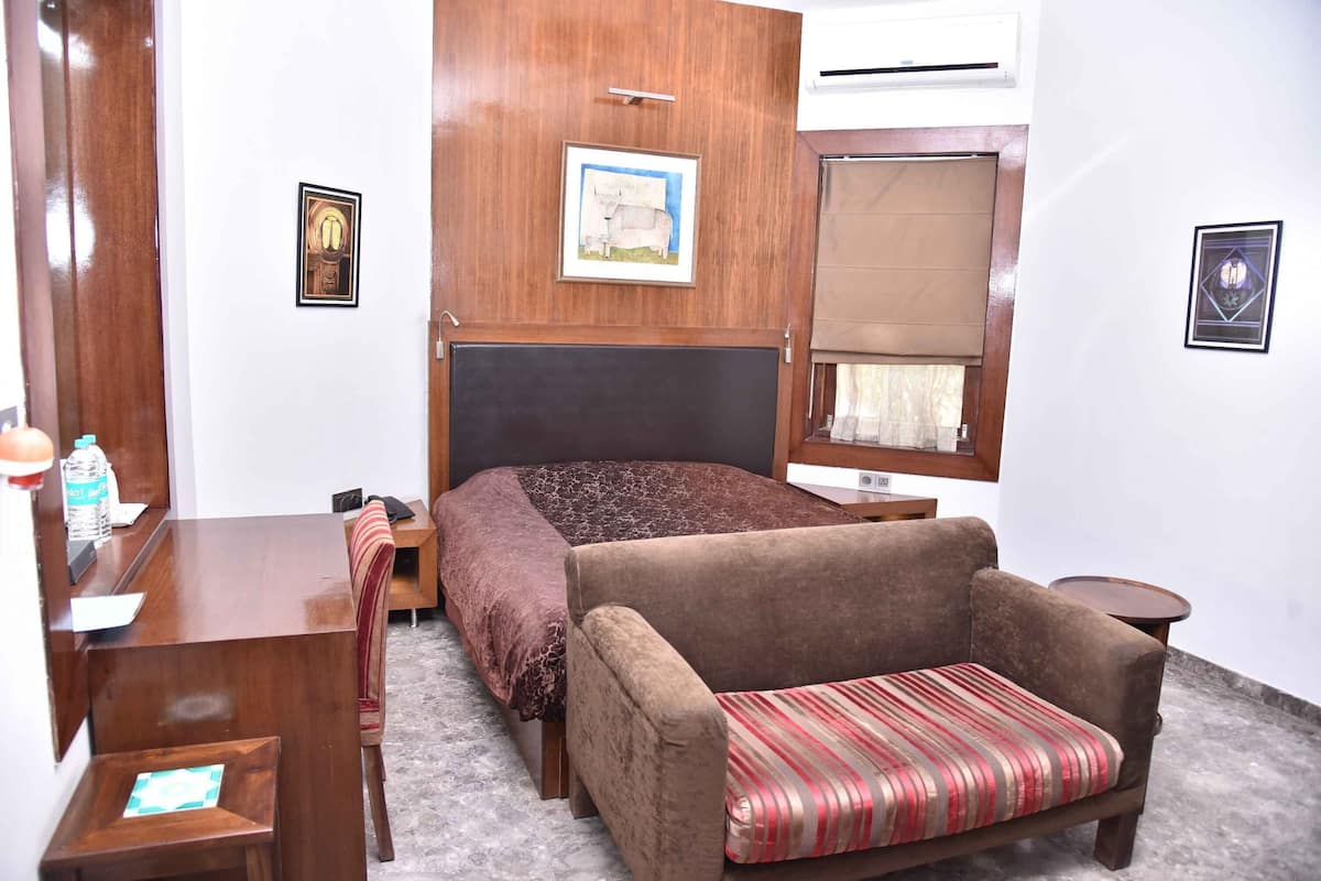 Quarto de hotel com escrivaninha de madeira, cama com colcha estampada, sofá com almofada listrada e janela com cortina.