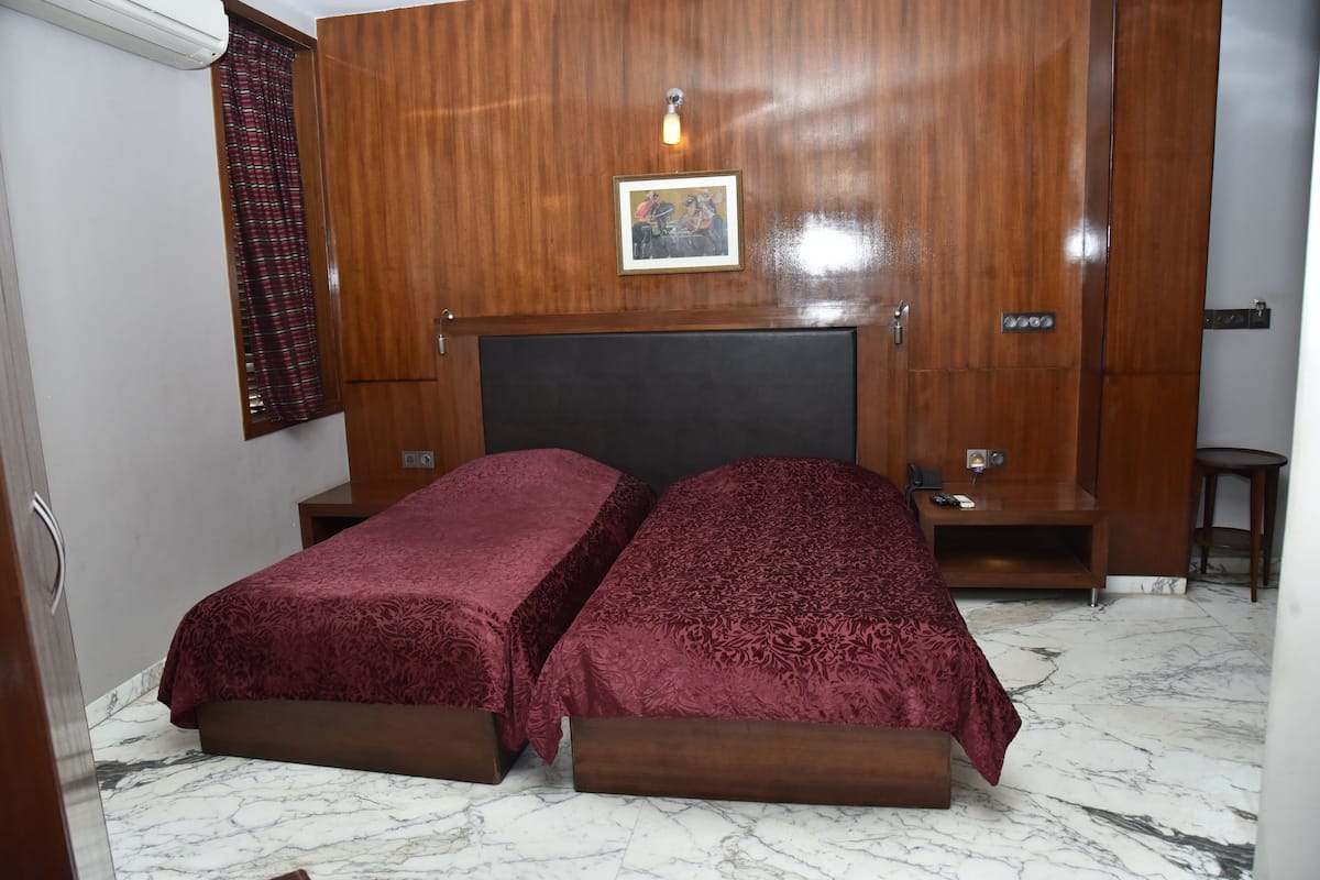 Quarto com duas camas, um guarda-roupa de madeira, um quadro na parede e uma mesinha de cabeceira com abajur.