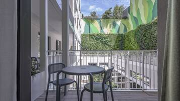 Uma varanda com mesa e cadeiras, guarda-corpo branco e parede verde coberta por plantas trepadeiras.