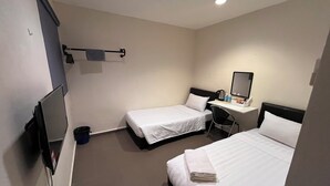 Quarto de hotel com duas camas de solteiro, uma escrivaninha com computador e uma televisão.