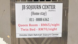 Um portão de metal com uma placa indicando JB SOJOURN CENTER, listando tarifas para Quarto de Rainha e Quartos Twin.