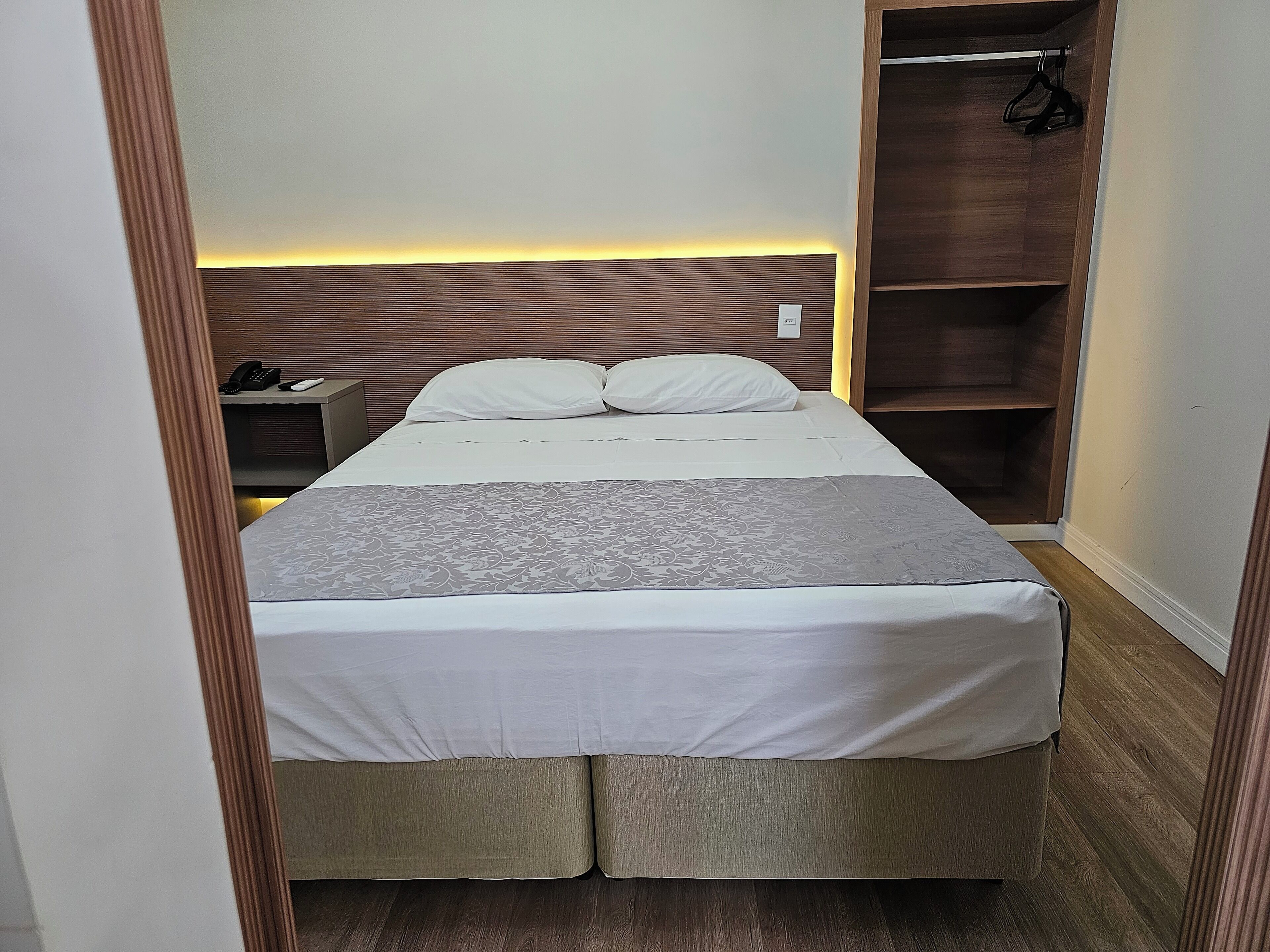 Uma cama bem arrumada com colcha estampada, mesa de cabeceira com telefone e cabeceira de madeira.