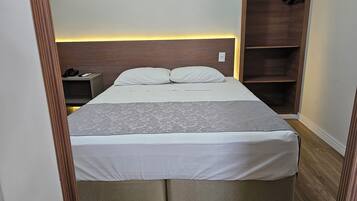 Uma cama bem arrumada com colcha estampada, mesa de cabeceira com telefone e cabeceira de madeira.