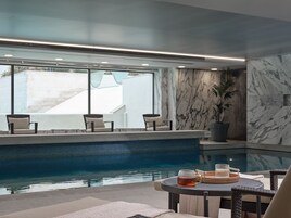 Área de piscina interna com assentos e uma mesa com bebida.