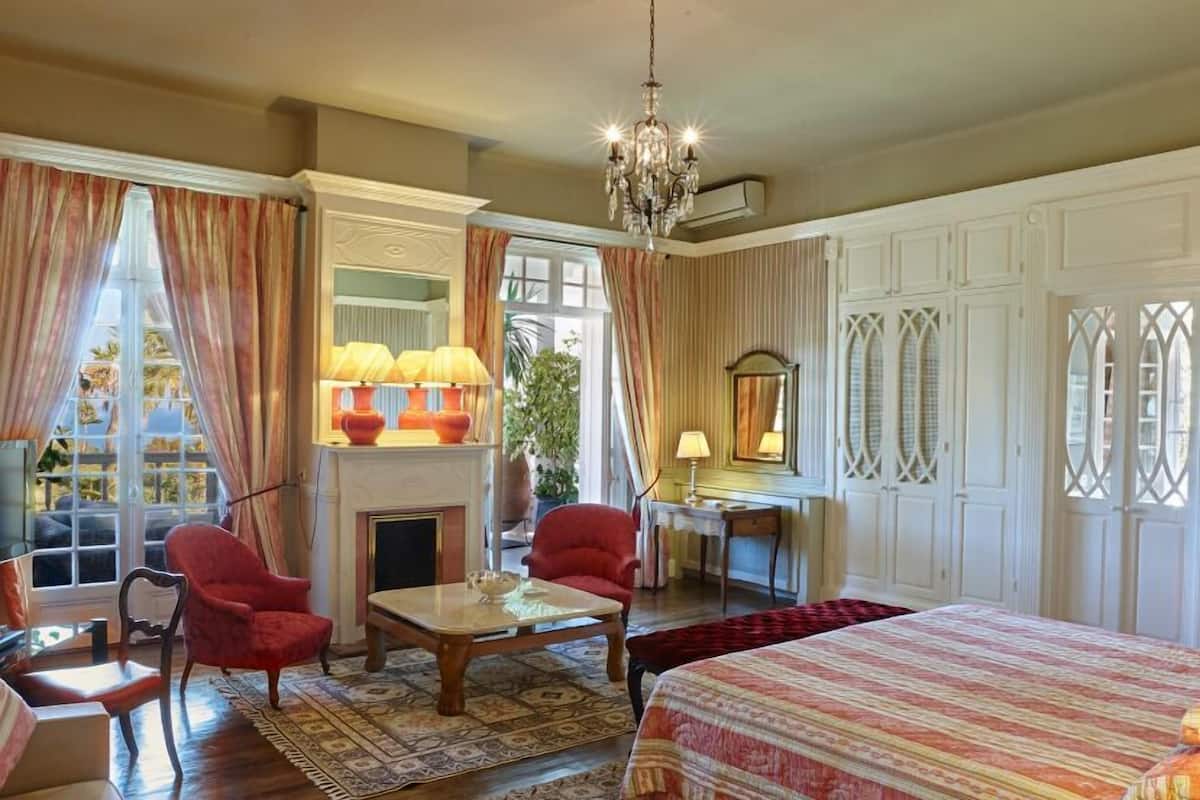 Um quarto espaçoso com uma cama grande, lareira, escrivaninha e um candelabro.