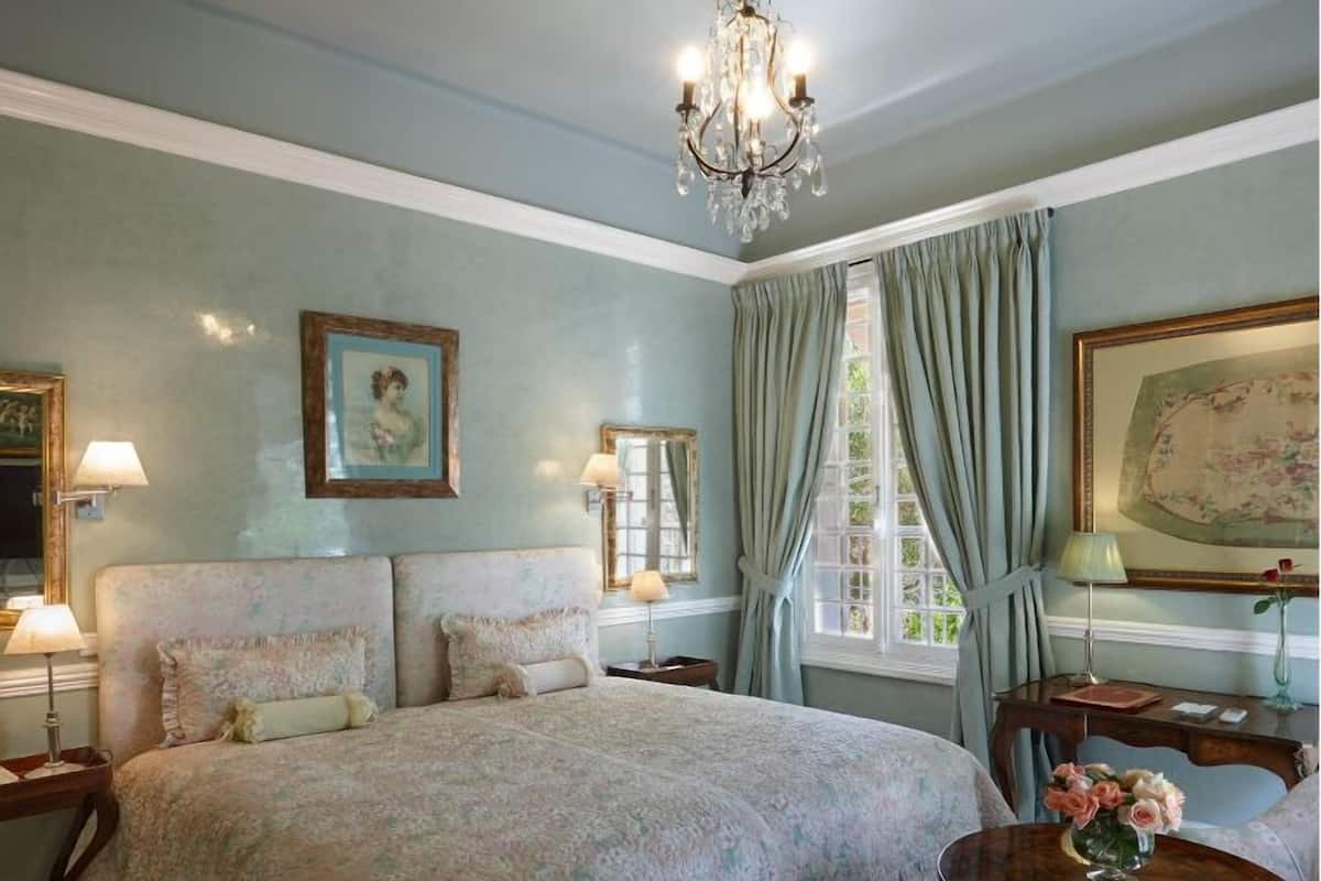 Um quarto espaçoso com uma cama grande, um candelabro, uma escrivaninha com um vaso de flores e uma cadeira.