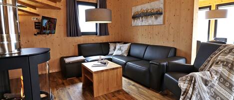 Interior acolhedor de uma cabana com piso de madeira, um sofá de couro preto, uma mesa de centro de madeira e uma lareira.