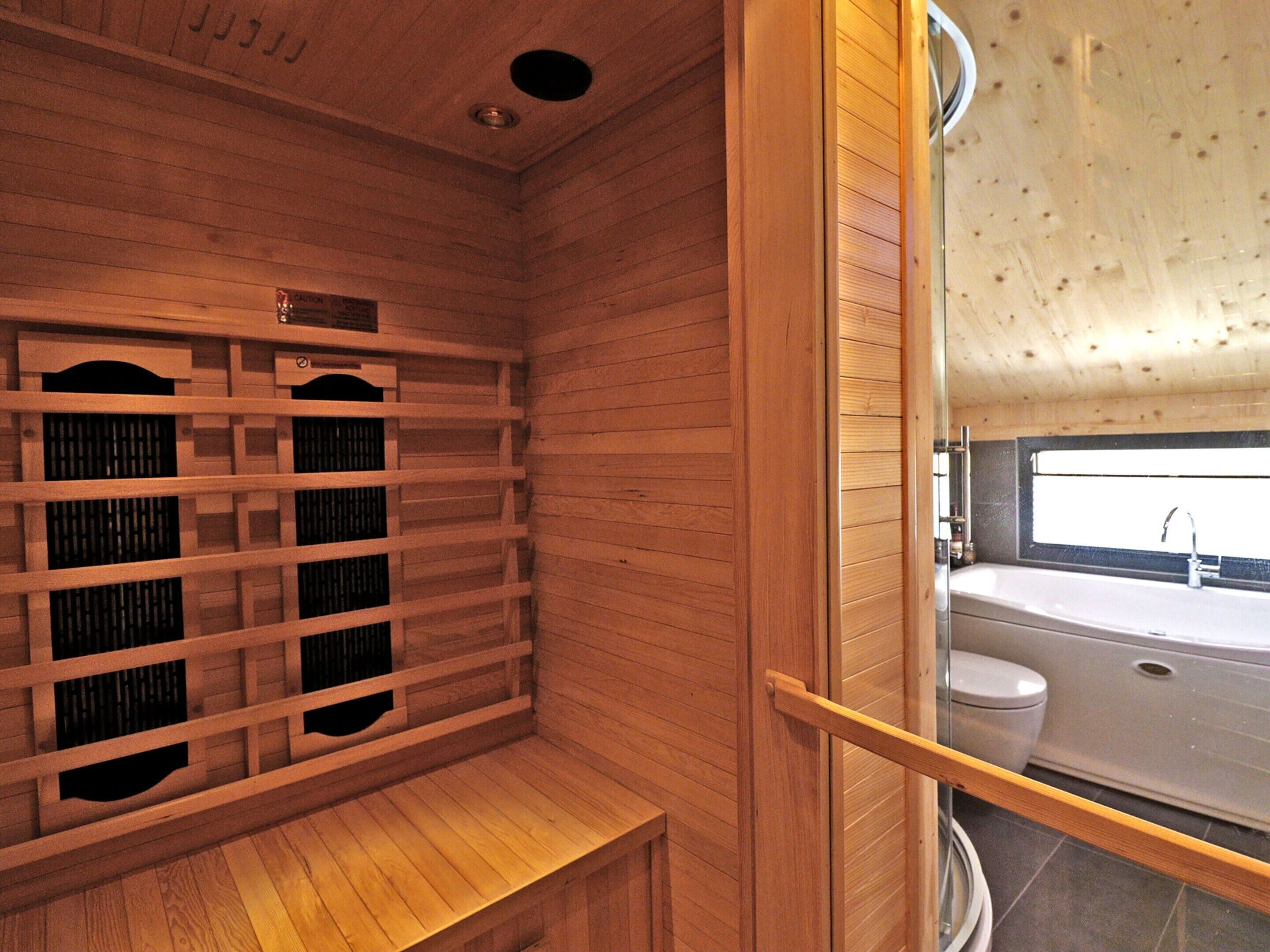 Uma sauna de madeira com um banco, uma janela e vista para um banheiro com banheira.