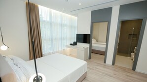 Quarto de hotel moderno com uma cama grande, mesa de cabeceira e televisão. Um banheiro é visível através de uma porta aberta.