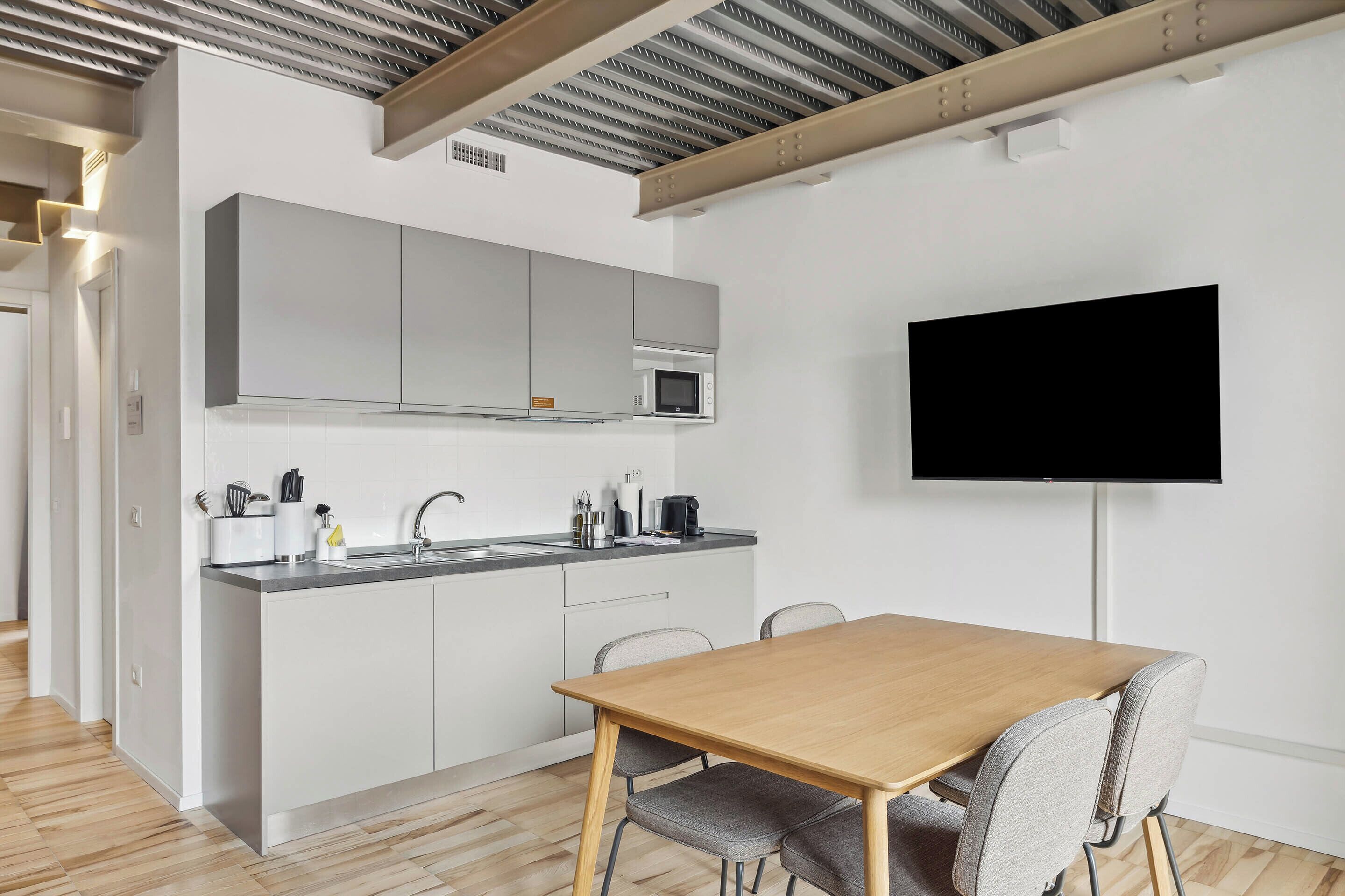 Cozinha moderna com armários brancos, micro-ondas e uma TV de tela plana na parede.