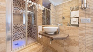 Uma casa de banho moderna com chuveiro envolto em vidro, uma pia grande e branca, e um porta-toalhas.
