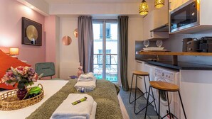 Quarto de hotel moderno com cama, área de refeições, cozinha e vista para a cidade.