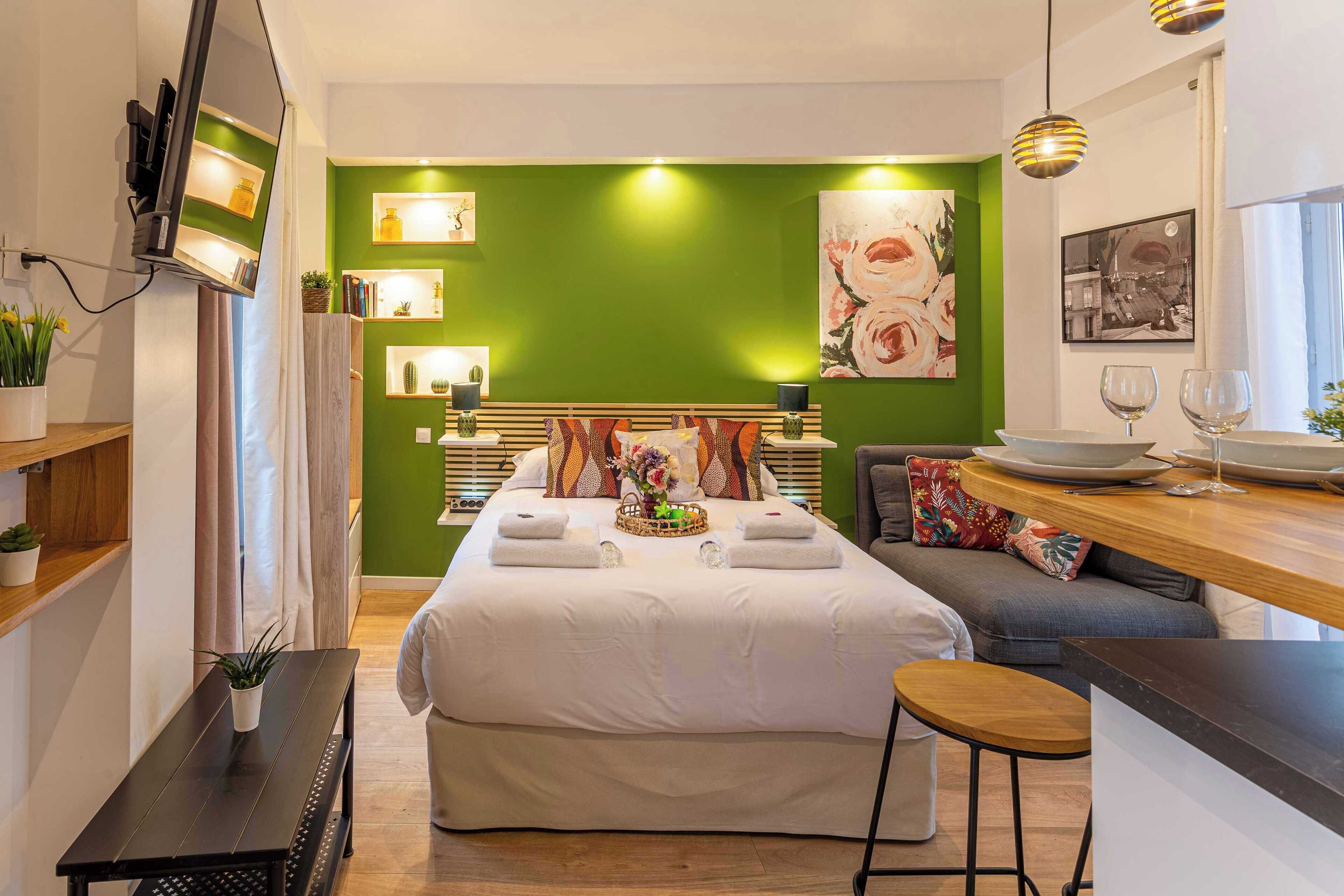 Quarto de hotel moderno com uma cama grande, área de refeições e uma parede verde.