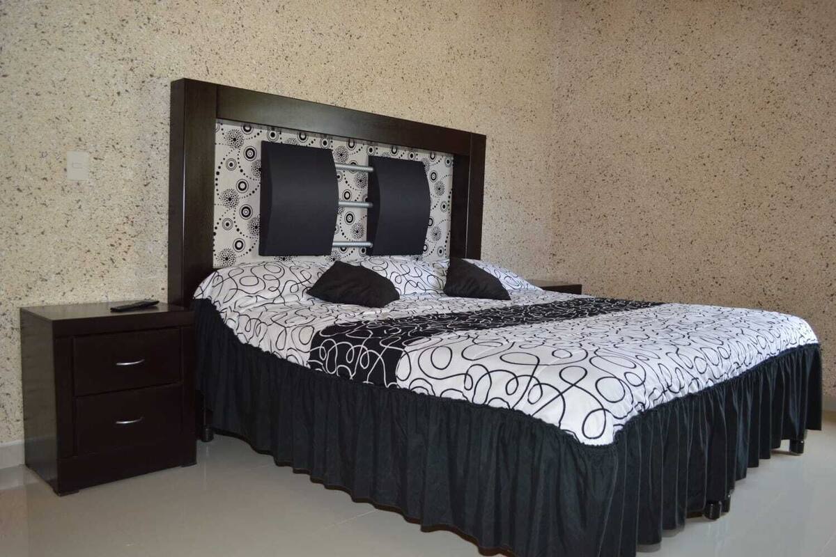 Quarto com cama, duas mesas de cabeceira, cômoda e parede estampada.