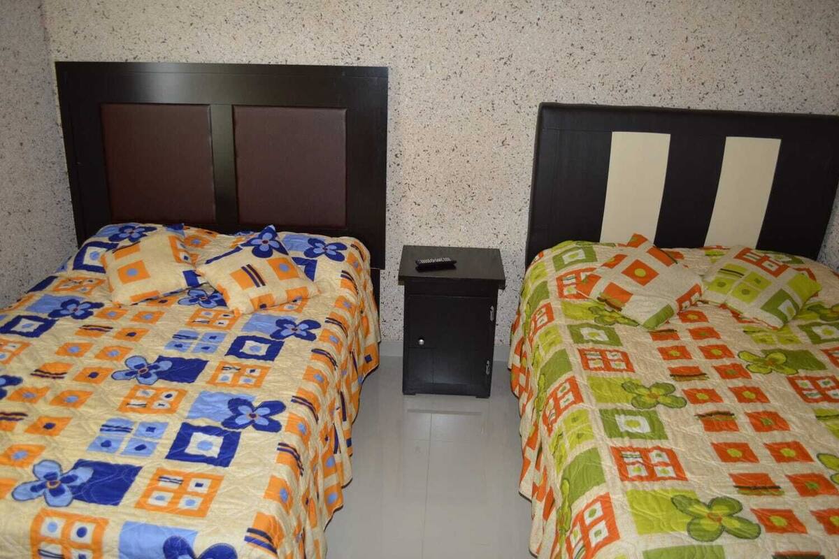 Duas camas com roupa de cama estampada em flores, uma pequena mesa de cabeceira preta e piso de azulejos.