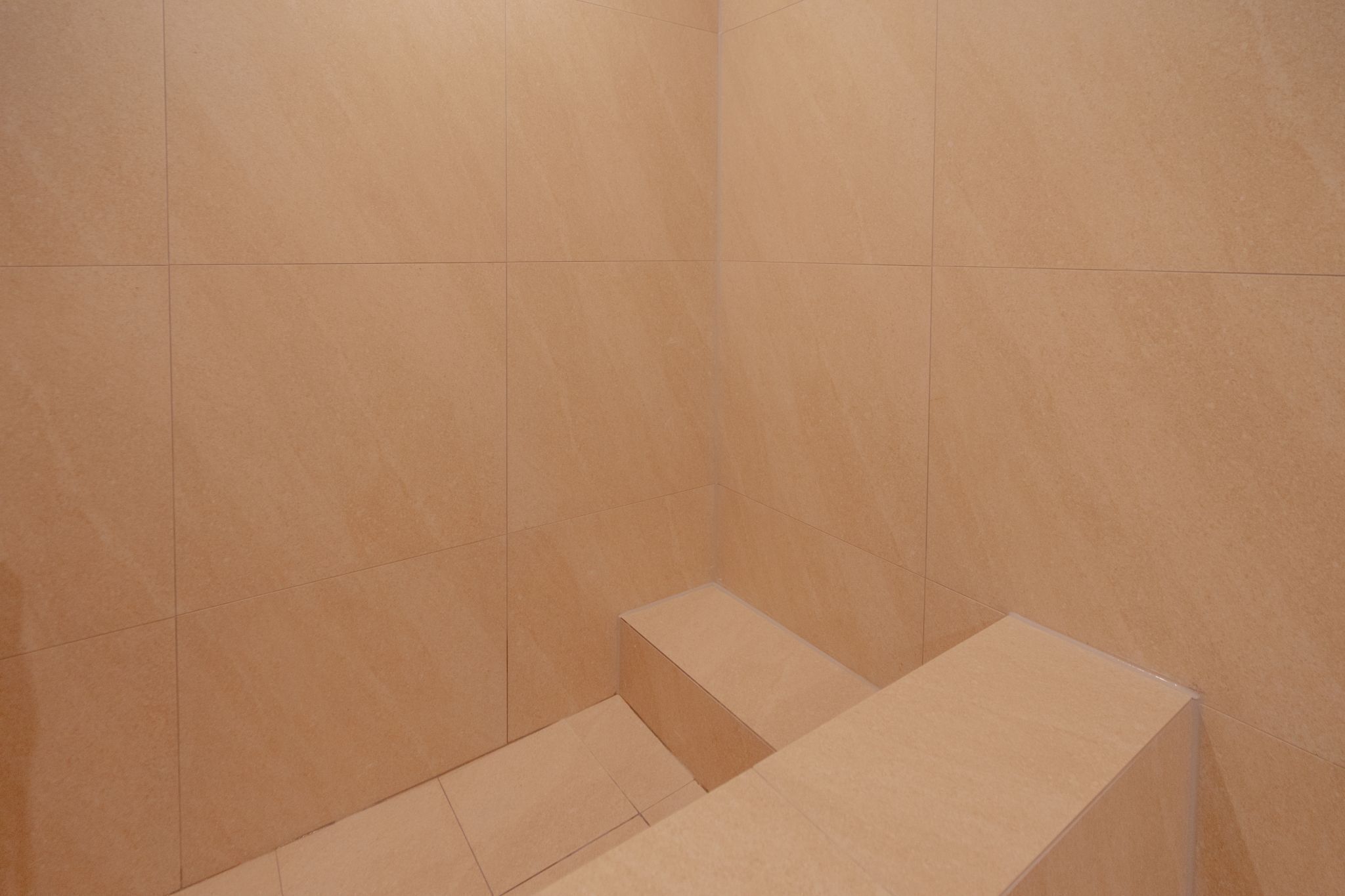 Um banheiro com azulejos bege e um pequeno degrau que dá acesso ao chuveiro.