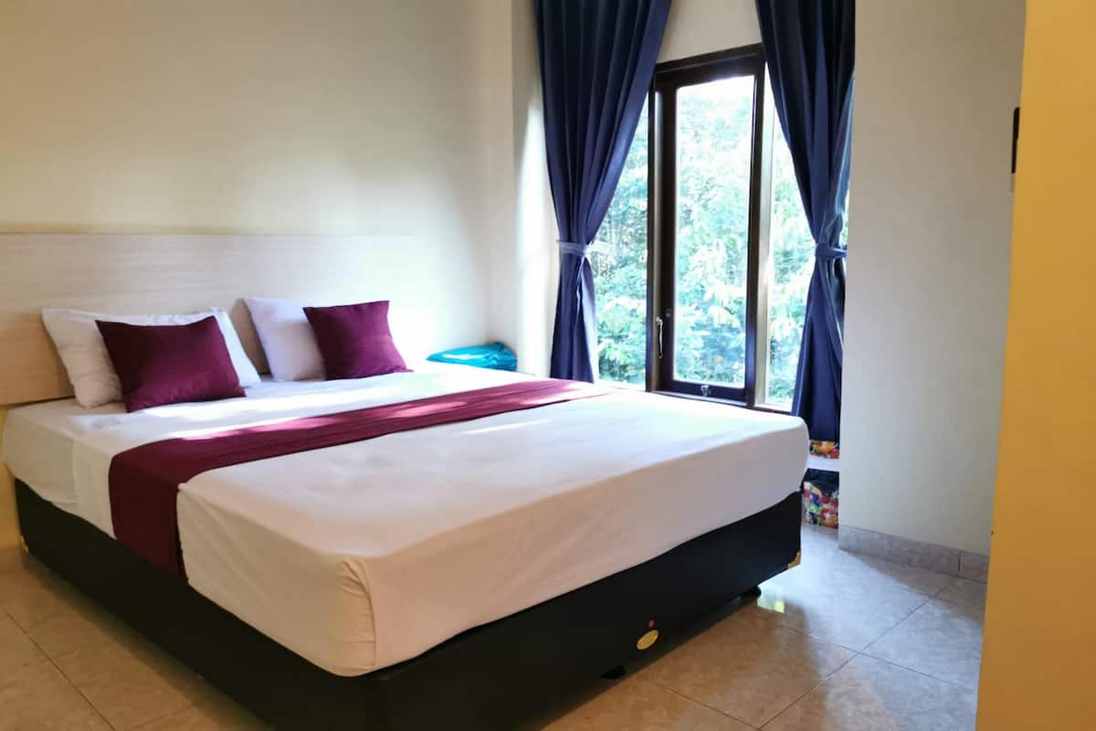 Cama bem arrumada com roupa de cama branca e roxa, cabeceira escura e janela com cortinas azuis.