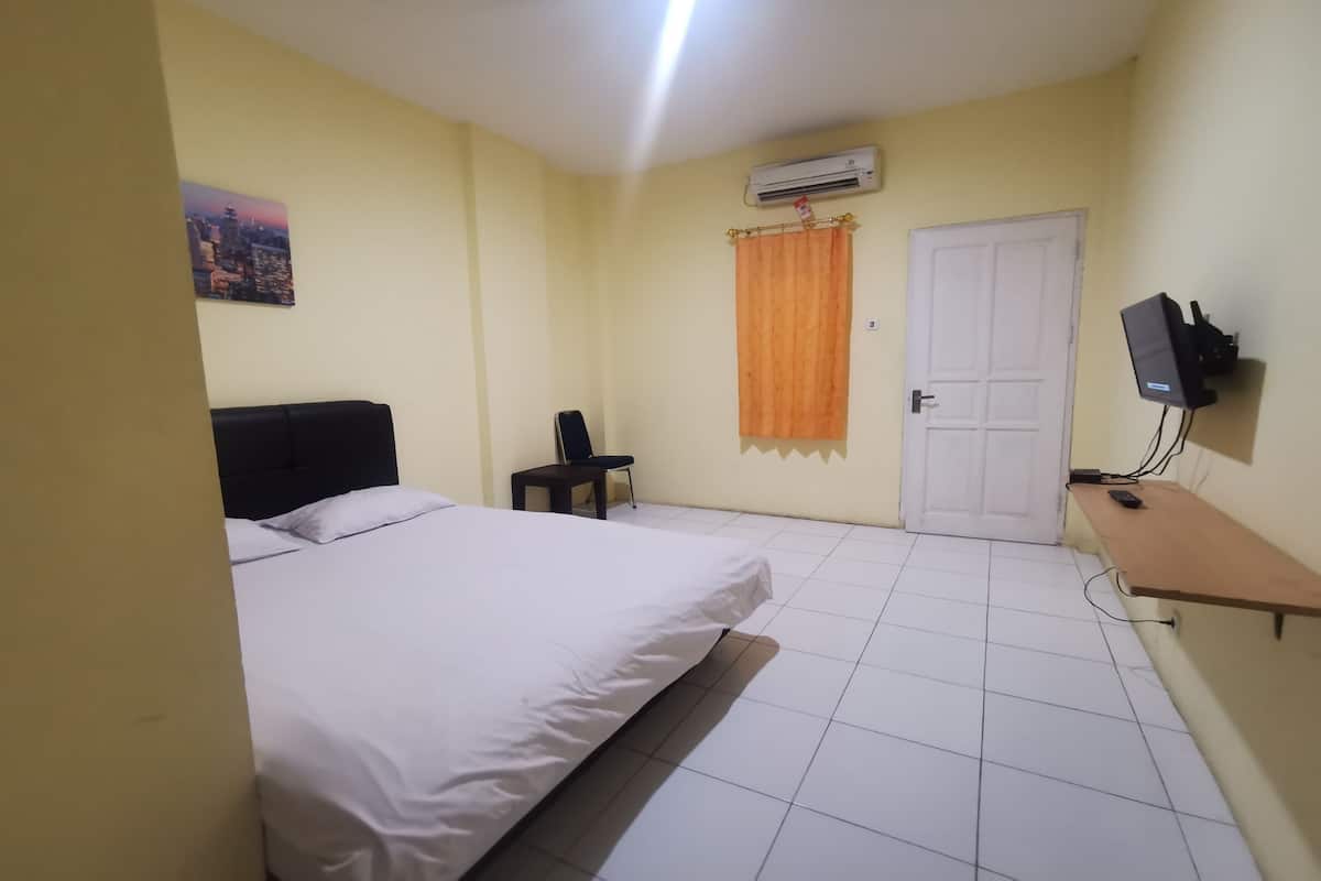 Quarto de hotel com uma cama, uma cadeira, ar-condicionado, uma porta e uma TV fixada na parede.