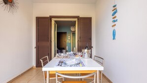 Uma sala de jantar com uma mesa branca posta para quatro pessoas, uma porta marrom e uma parede decorada com enfeites de peixe.