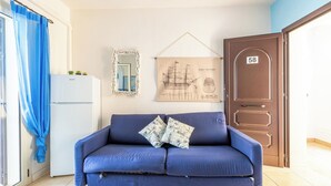 Um quarto com um sofá azul, uma geladeira branca, uma porta com o número 58 e um mapa emoldurado na parede.